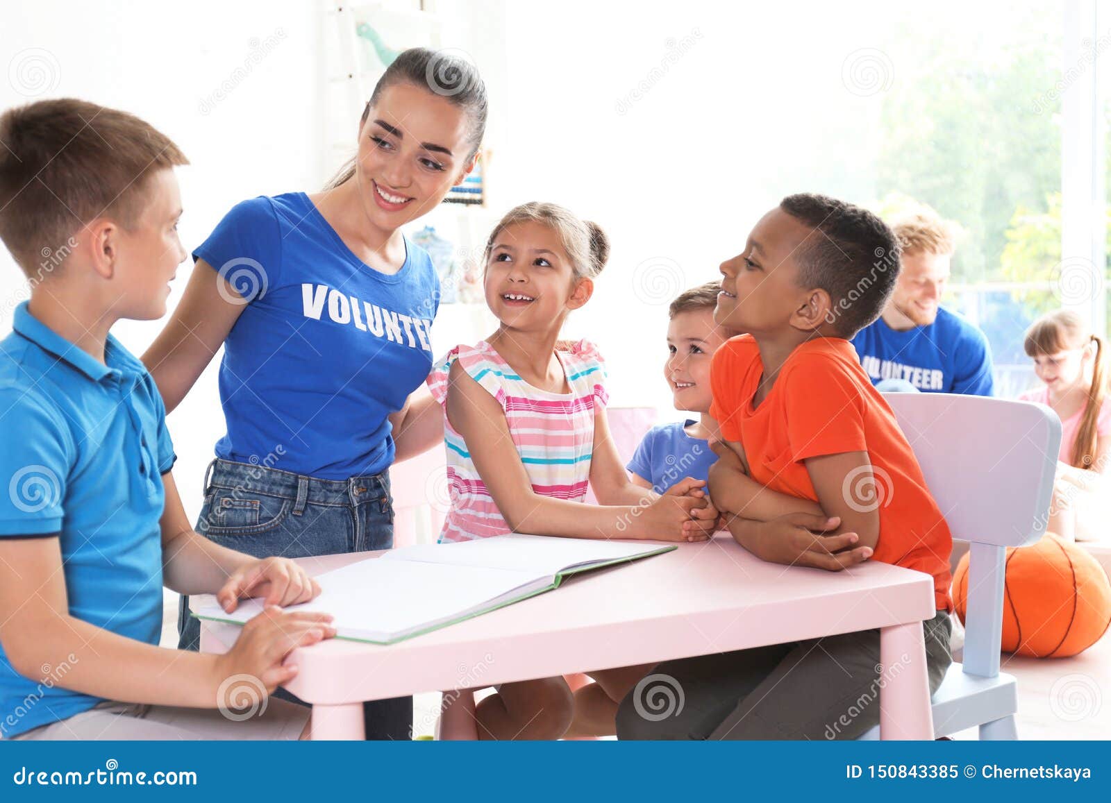 Young Volunteer Reading Book with Children at Table Stock Image - Image ...