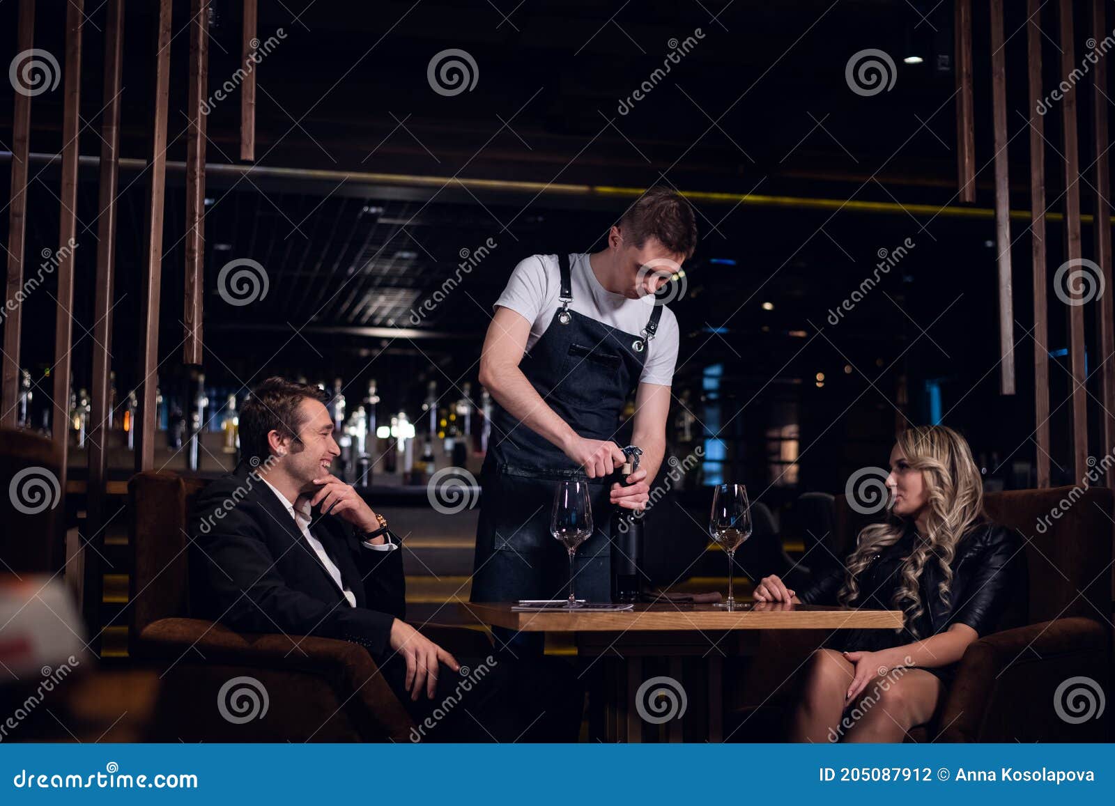 A Young Waiter Guy Opens a Bottle of Wine at the Table in a Restaurant ...