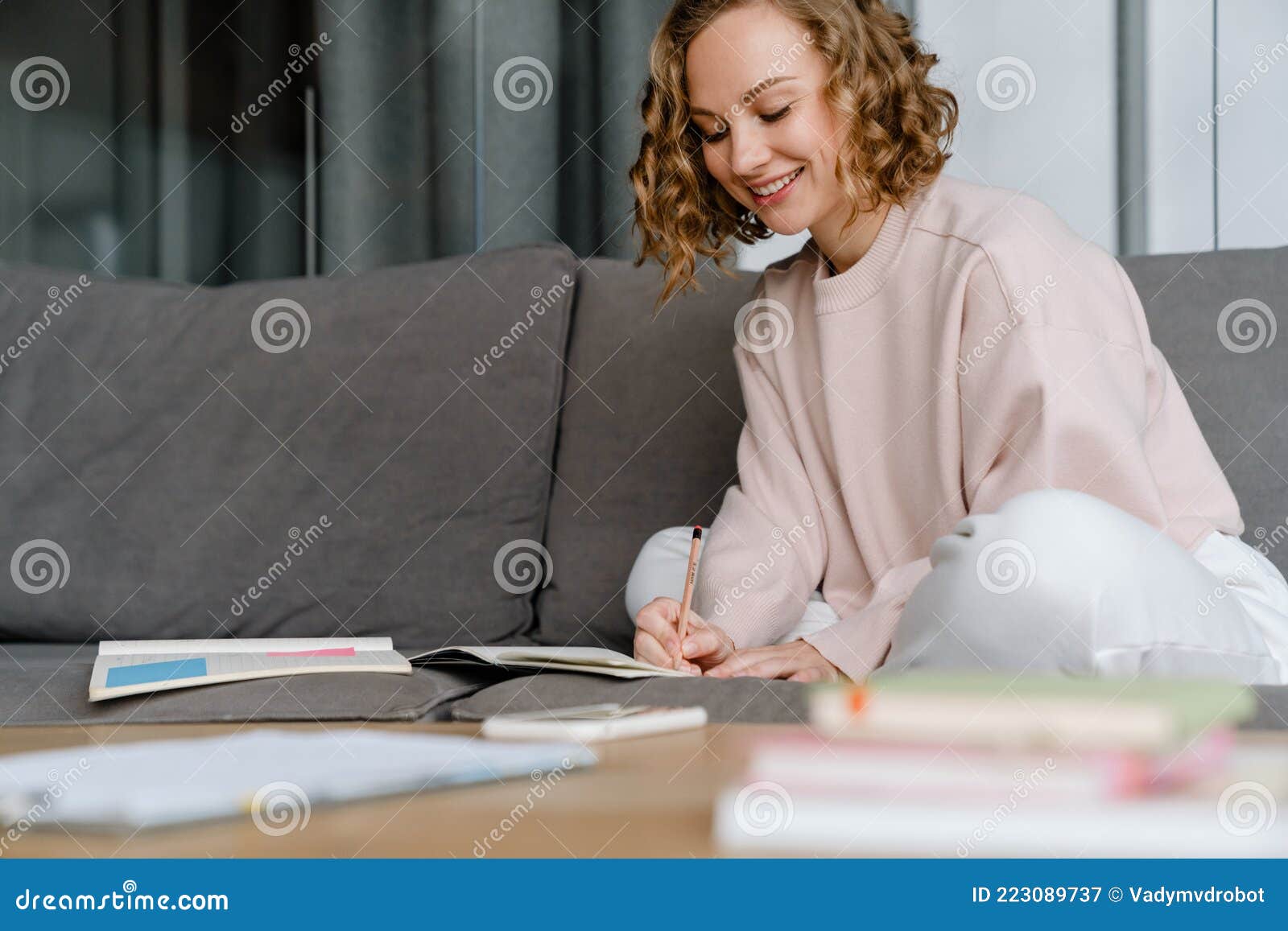 Young White Woman Smiling and Writing Down Notes while Sitting on Couch ...