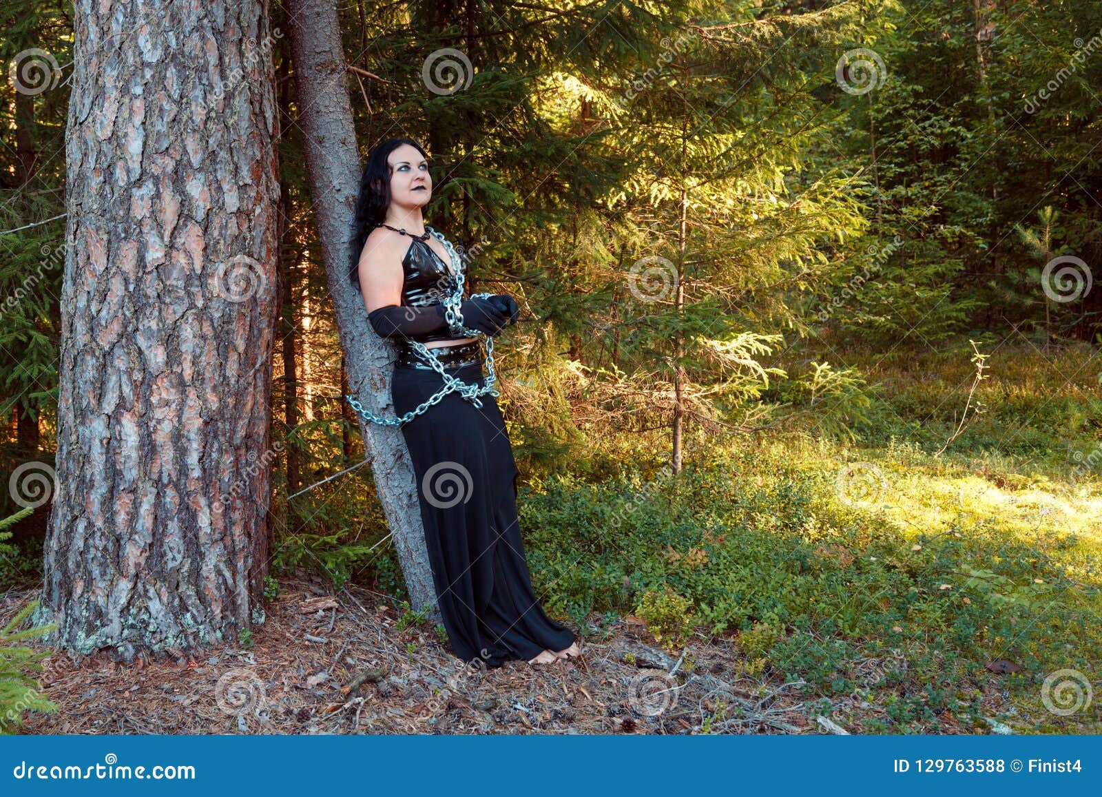 A Young Witch in Black Clothes is Chained To a Tree. Halloween ...