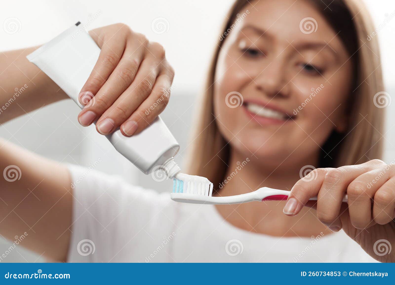 Young Woman Applying Toothpaste Onto Brush In Bathroom Focus On Hands
