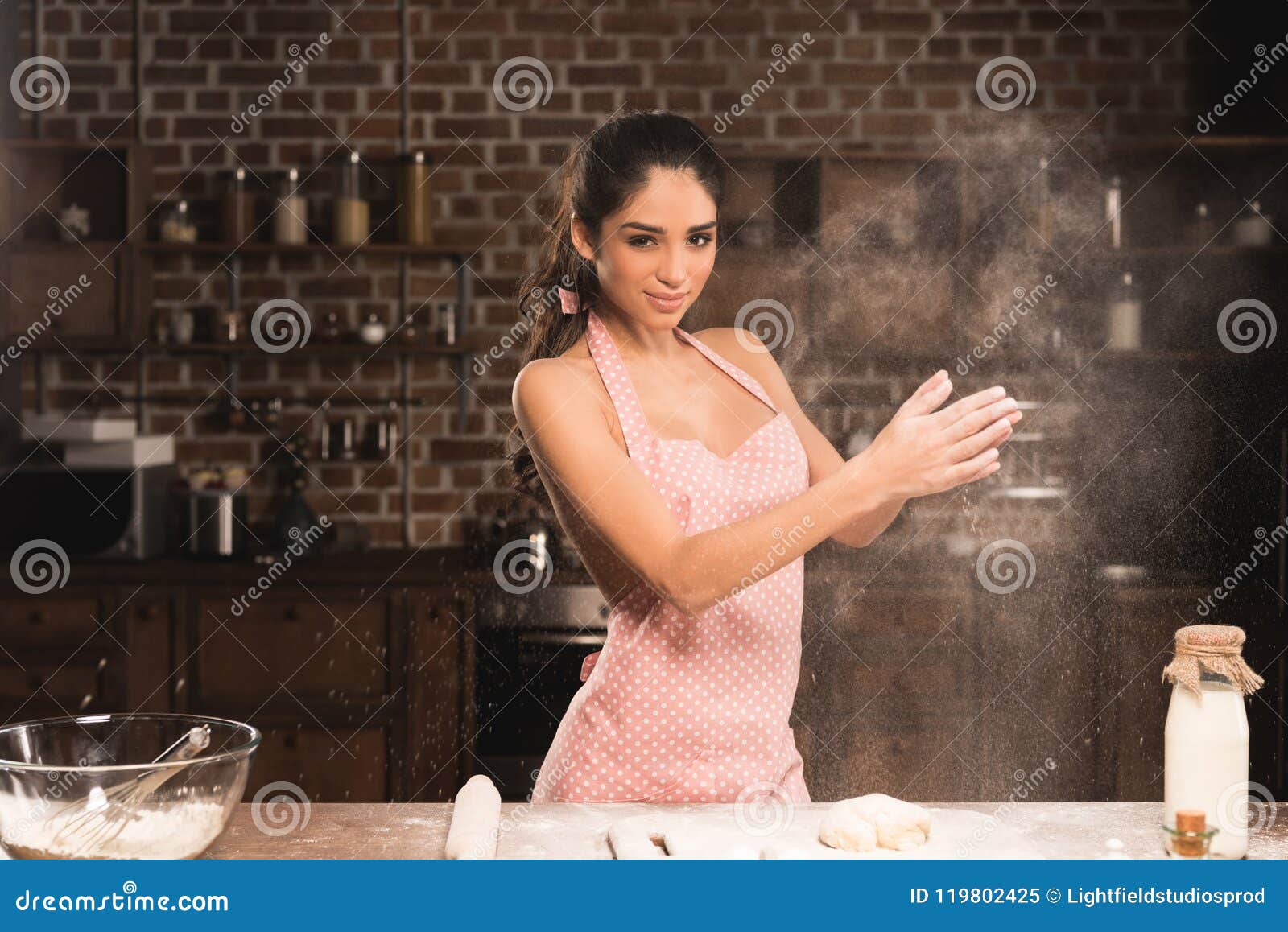 Young Woman In Apron Clapping Hands With Flour And Smiling At Camera While Cooking Stock Image