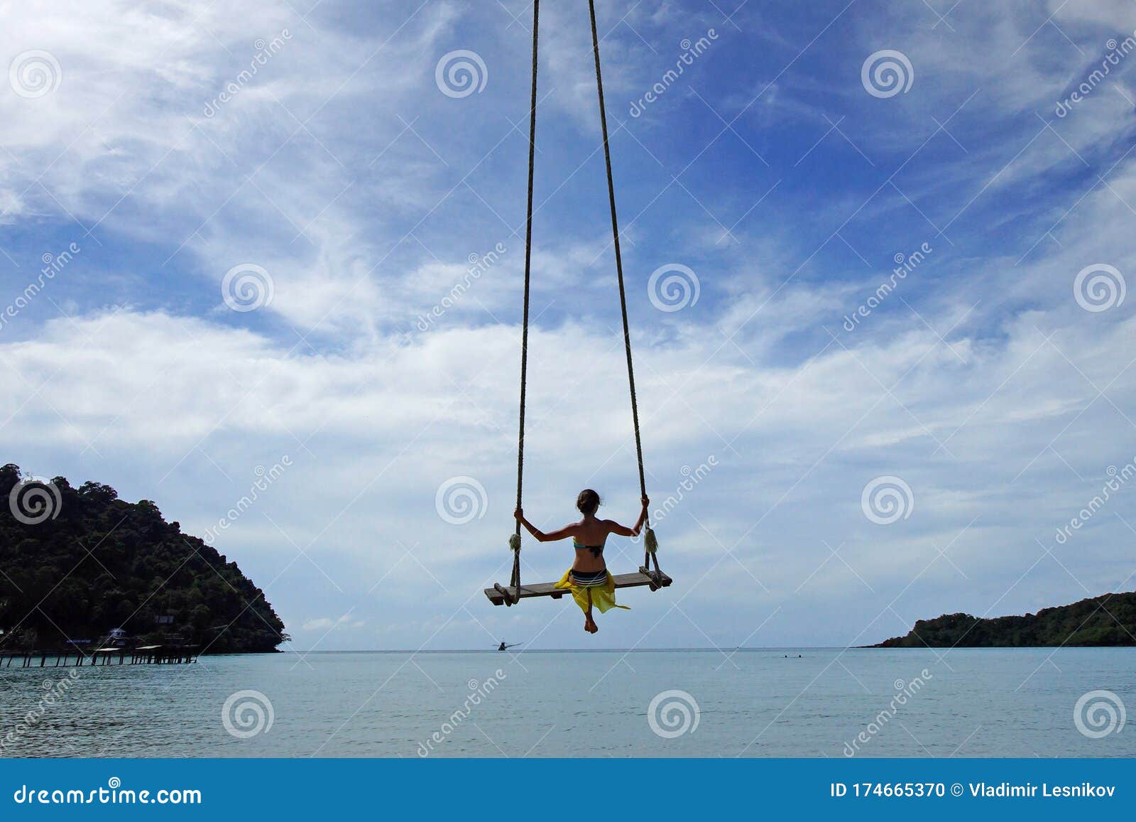 Young Woman In Bikini Swinging On Rope Swing Over Ocean Water On