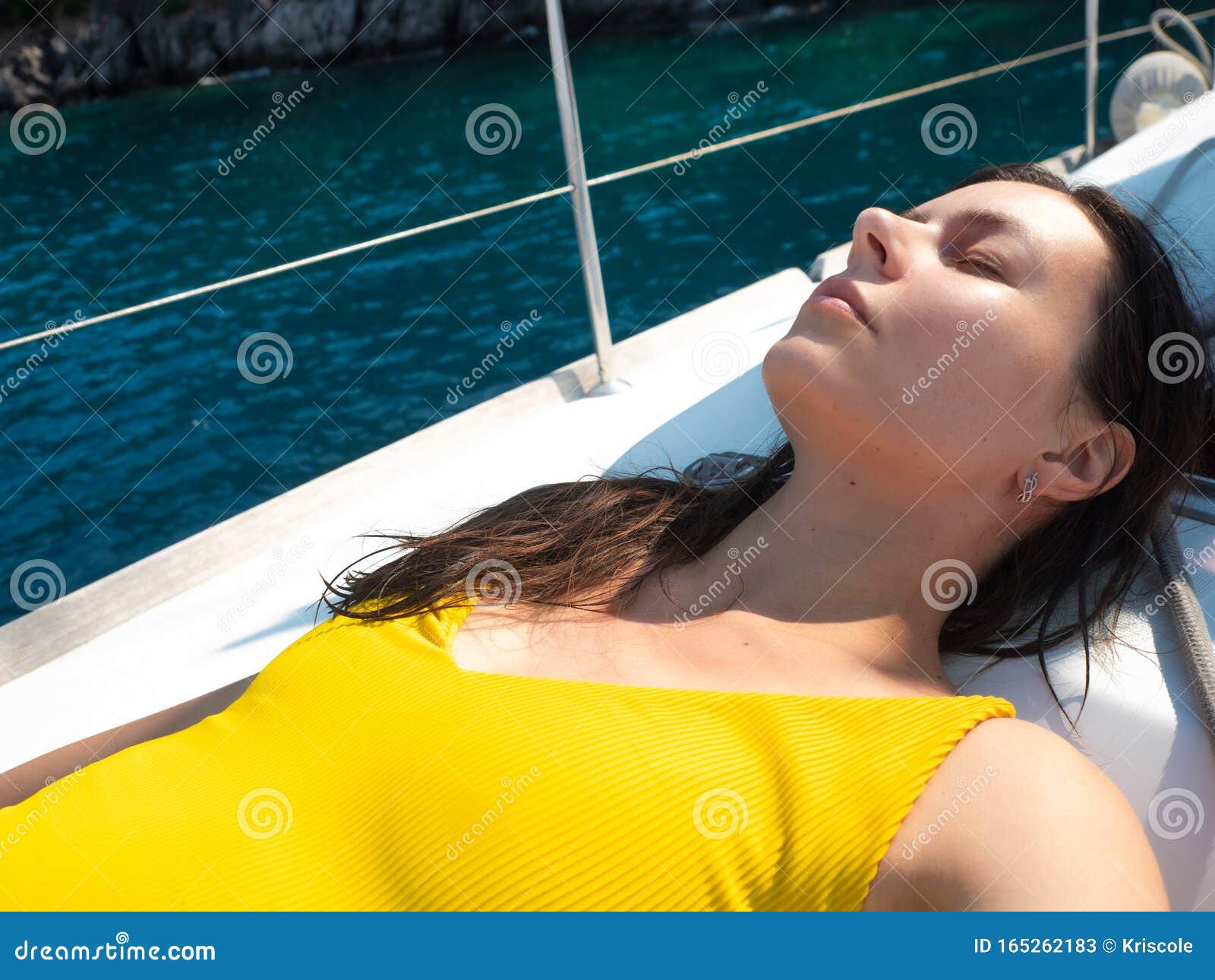 Young Woman In A Bright Yellow One Piece Swimsuit Sunbathing On The