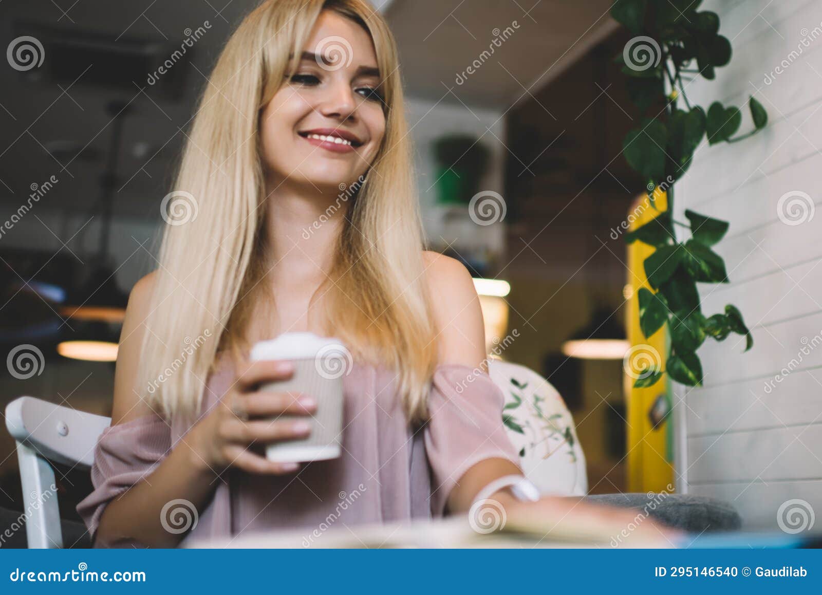 Young Woman Drinking Coffee And Smiling While Sitting In Cafe And