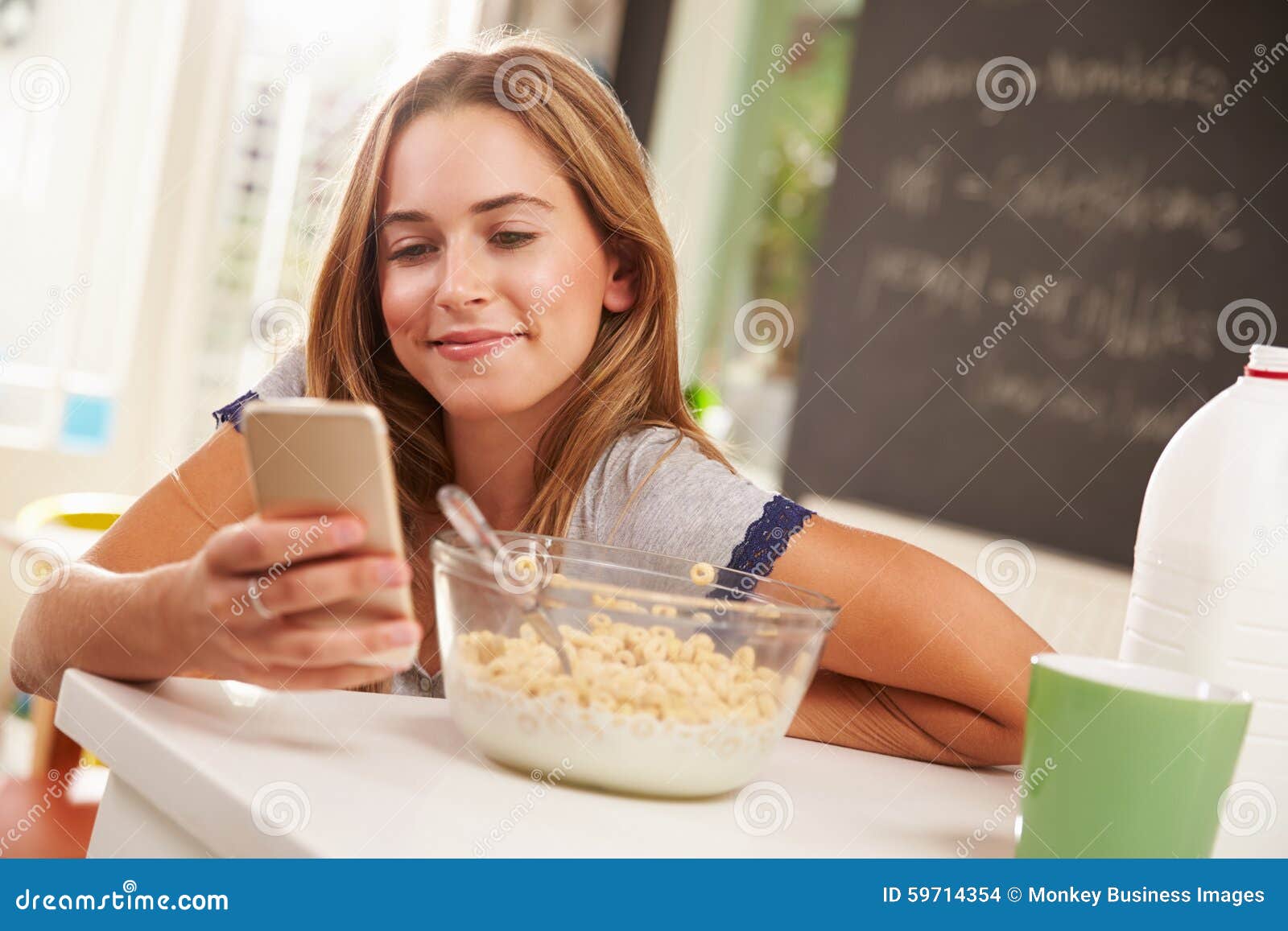 Young Woman Eating Breakfast Whilst Using Mobile Phone Stock Photo ...