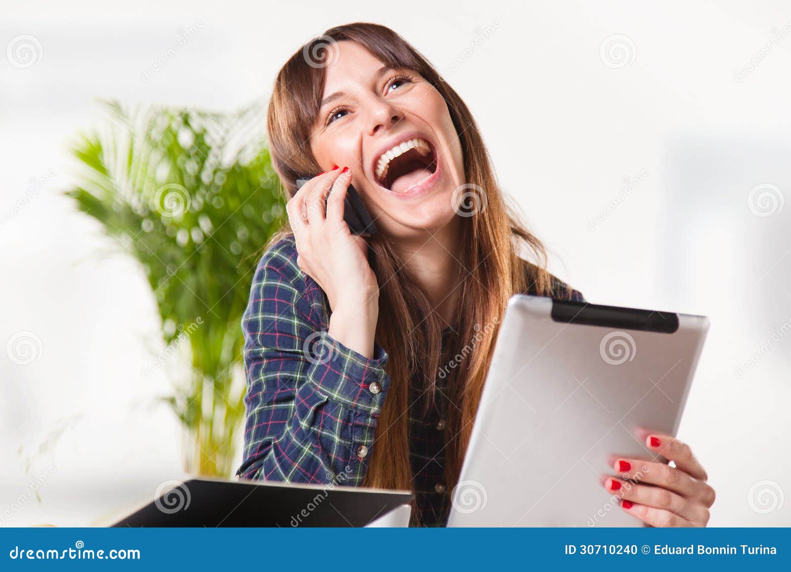 Young Woman Laughing with a Phone and a Tablet in the Office Stock ...