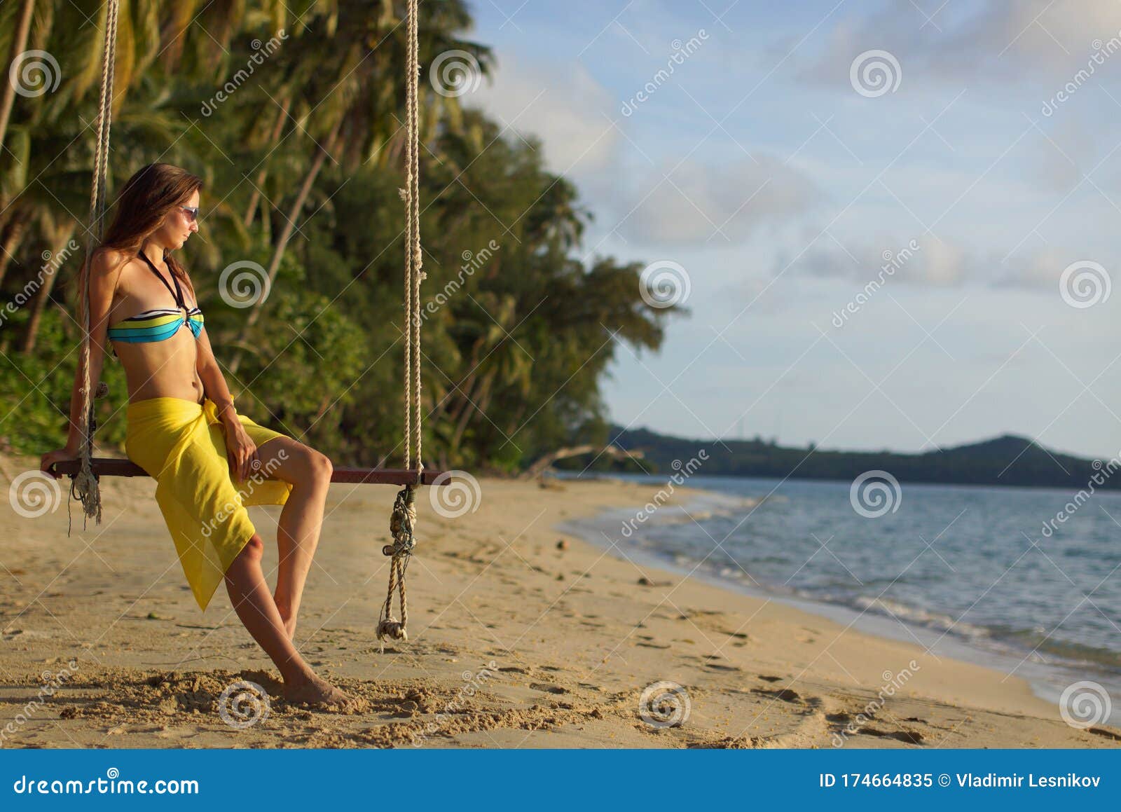 Young Woman With Long Hair In Bikini Sitting On Rope Swing On Tropical