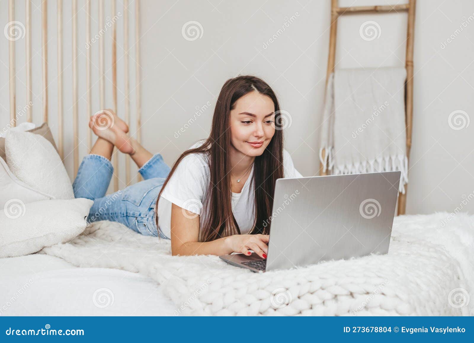 Young Woman Lying On Her Stomach In Bed Work On Laptop And Takes Online