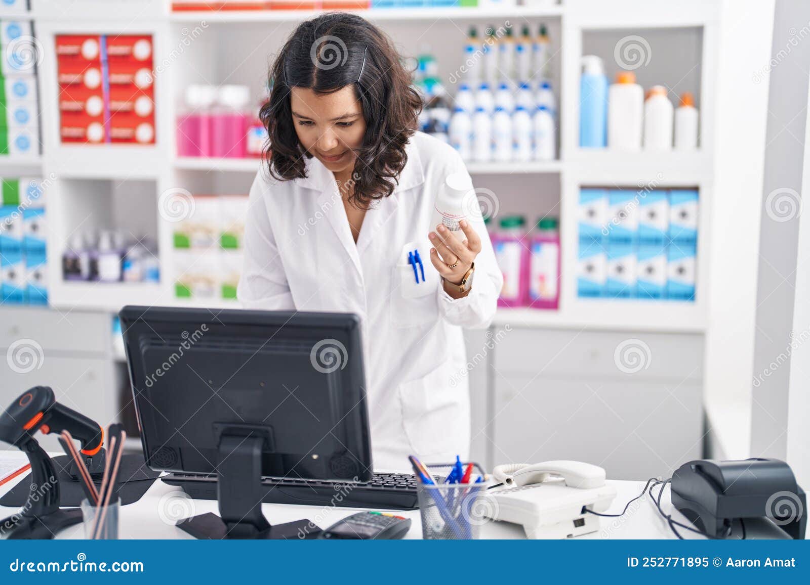 Young Woman Pharmacist Holding Pills Bottle Using Computer at Pharmacy ...