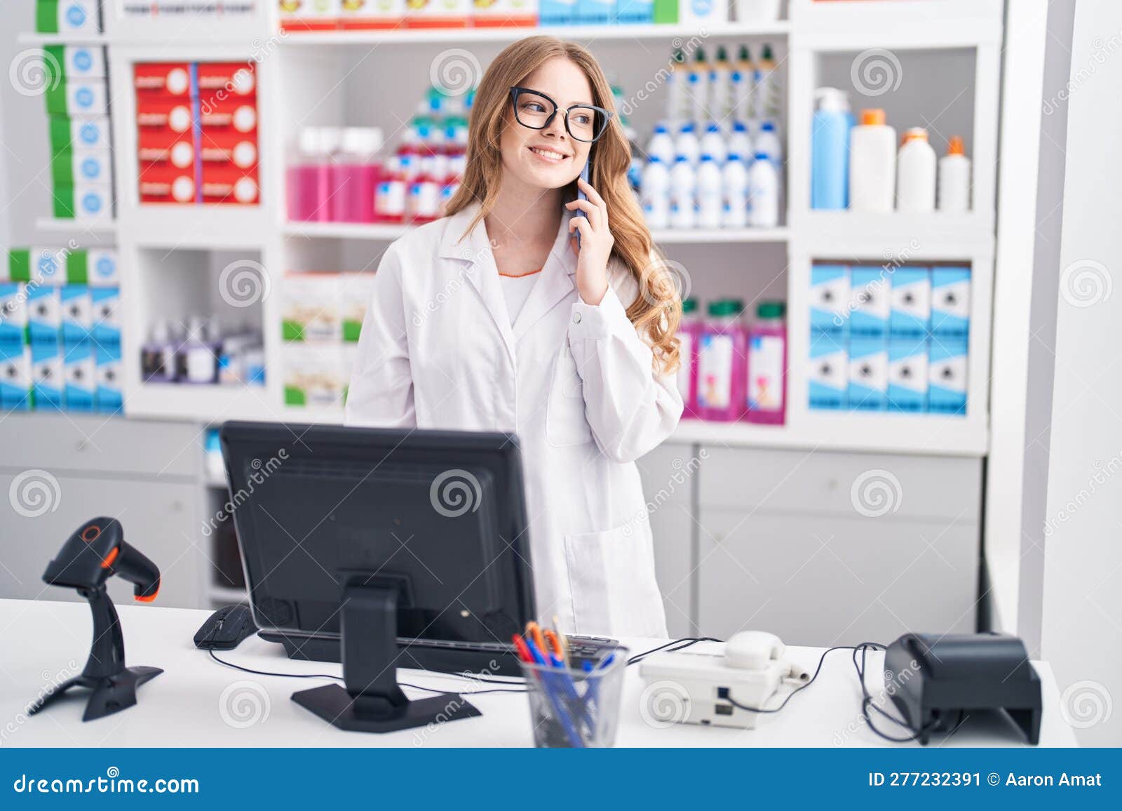 Young Woman Pharmacist Talking on Smartphone Using Computer at Pharmacy ...