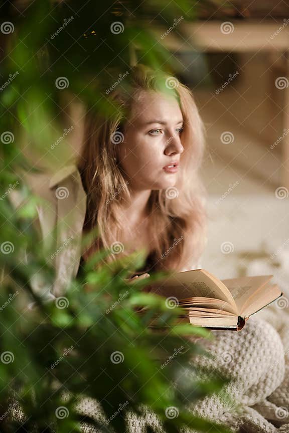 Young Woman Reading A Book While Sitting On Her Bed At Home In The
