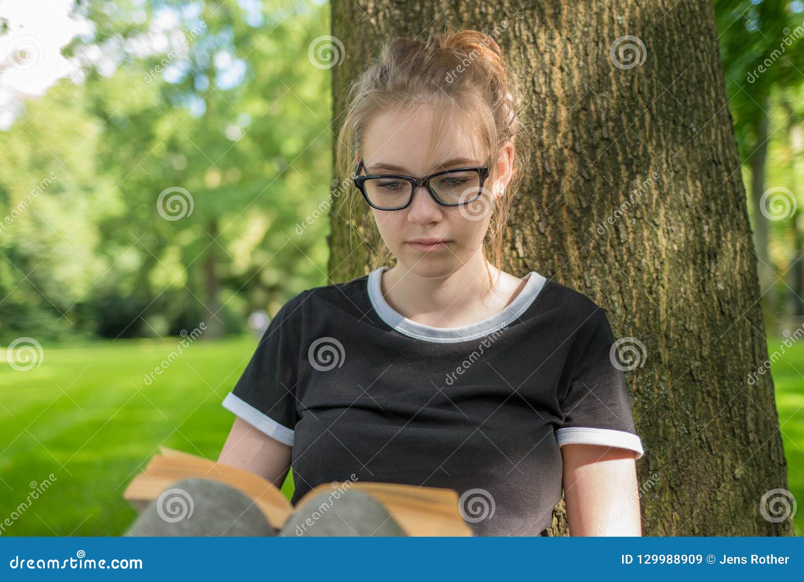 A Young Woman Sits Under a Tree in a Park and Read a Book Stock Image ...