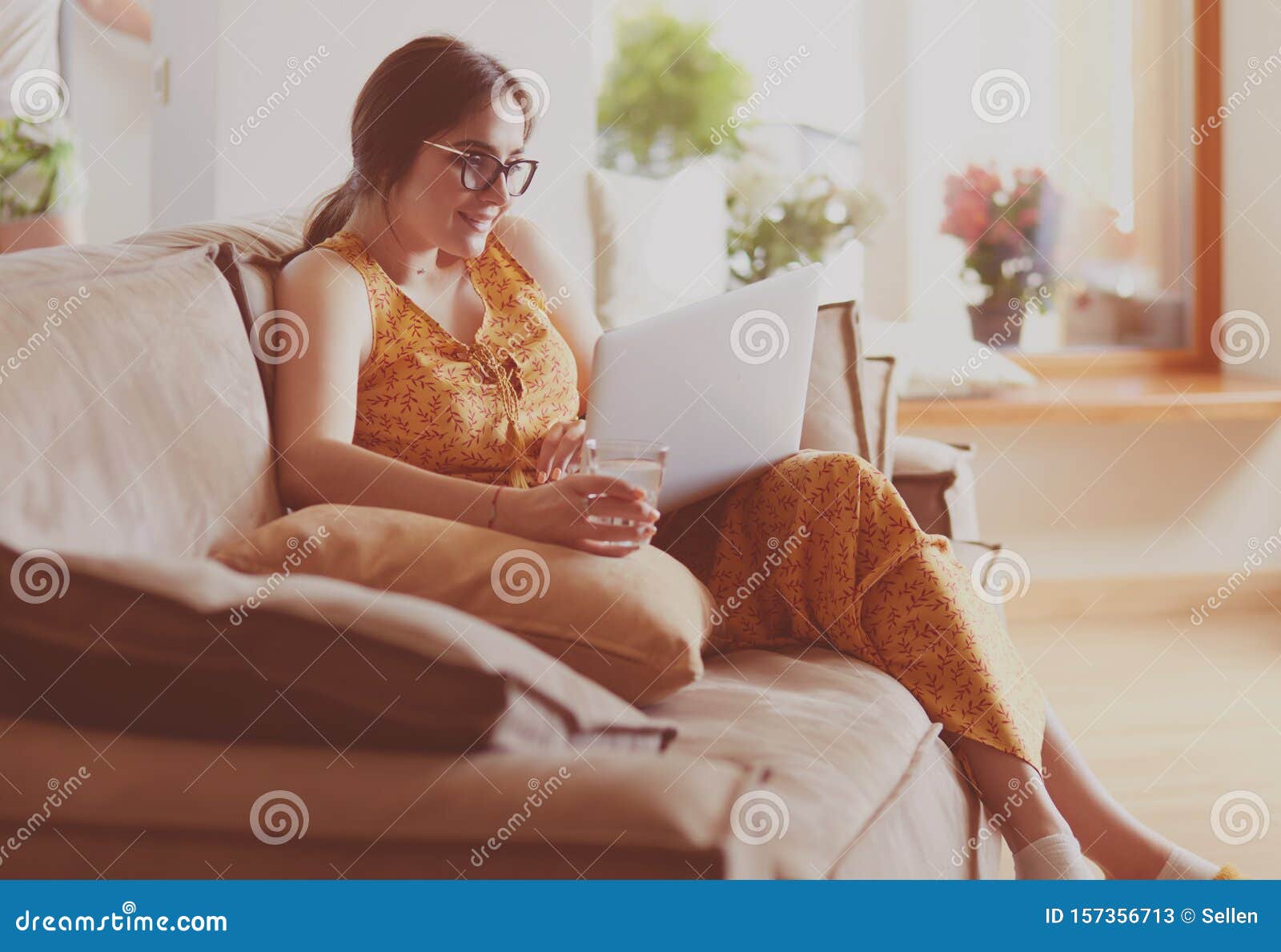 Young Woman Sitting On Couch Working On Laptop Computer At Home Stock