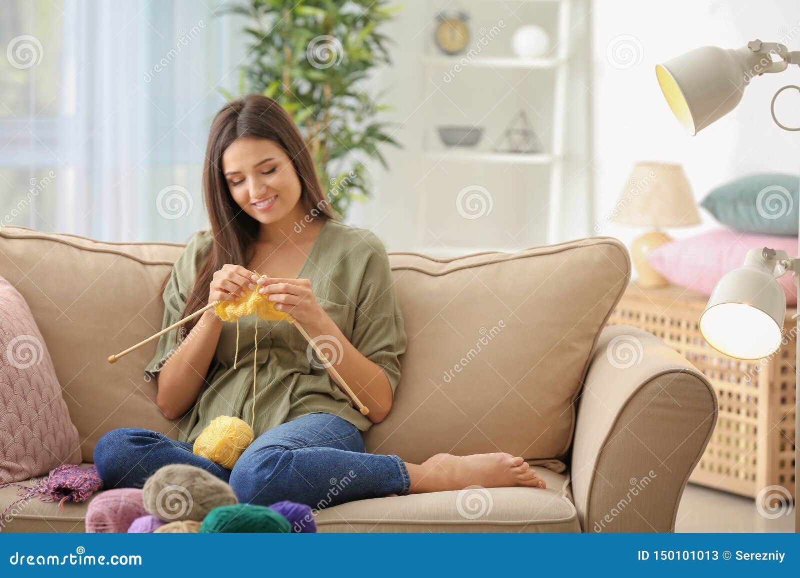 Young Woman Sitting On Sofa And Knitting Warm Sweater Indoors Stock