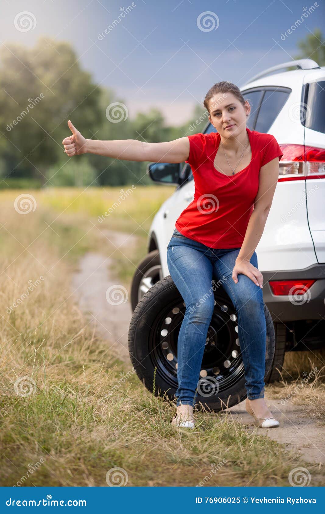 Young Woman Sitting On Spare Tire At Broken Car And Hitchhiking Stock