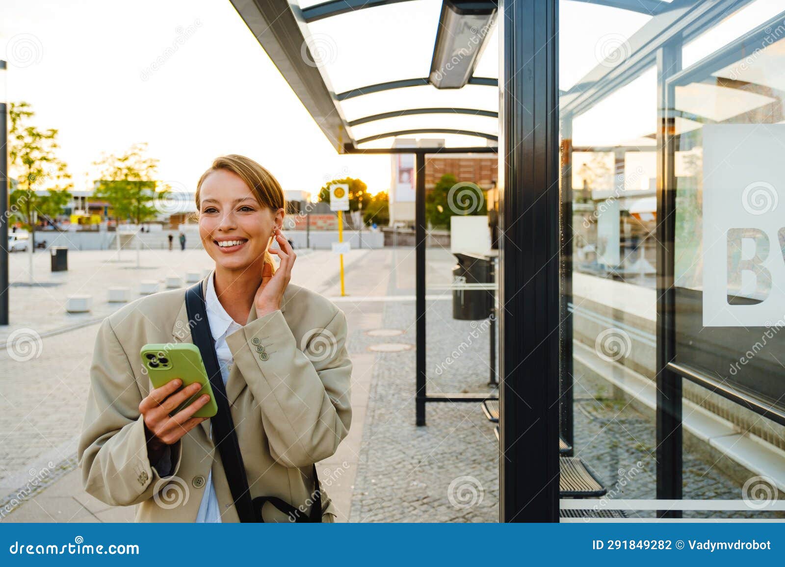 Young Woman Smiling and Using Cellphone while Standing at Bus Station ...