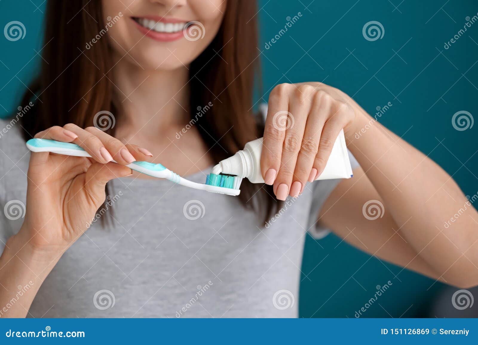 Young Woman Squeezing Toothpaste on Brush Against Color Background ...