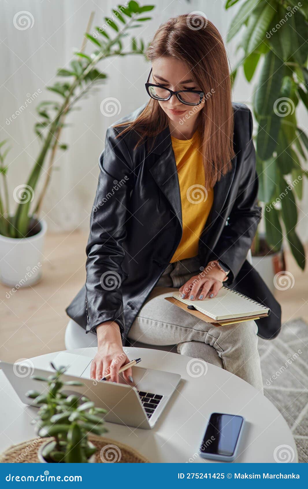 Young Woman Using Laptop And Making Notes In Notebook Sitting At