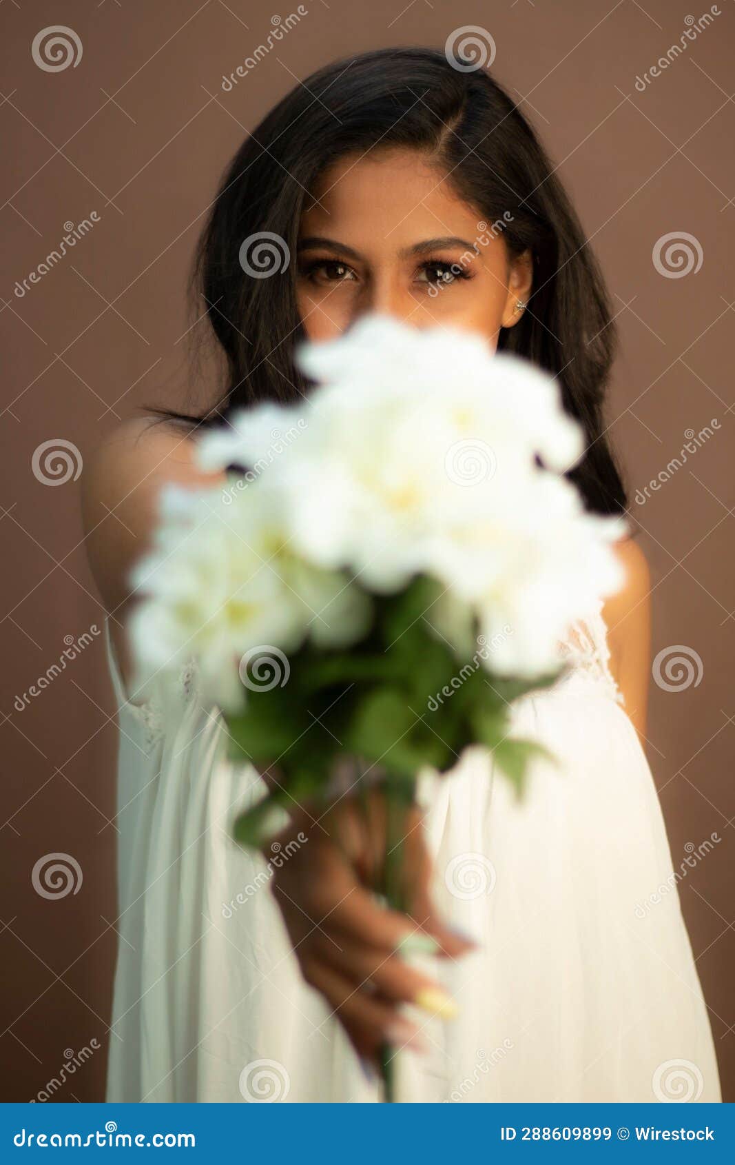 Young Woman In A White Dress Holding A Bouquet Of White Flowers Up To