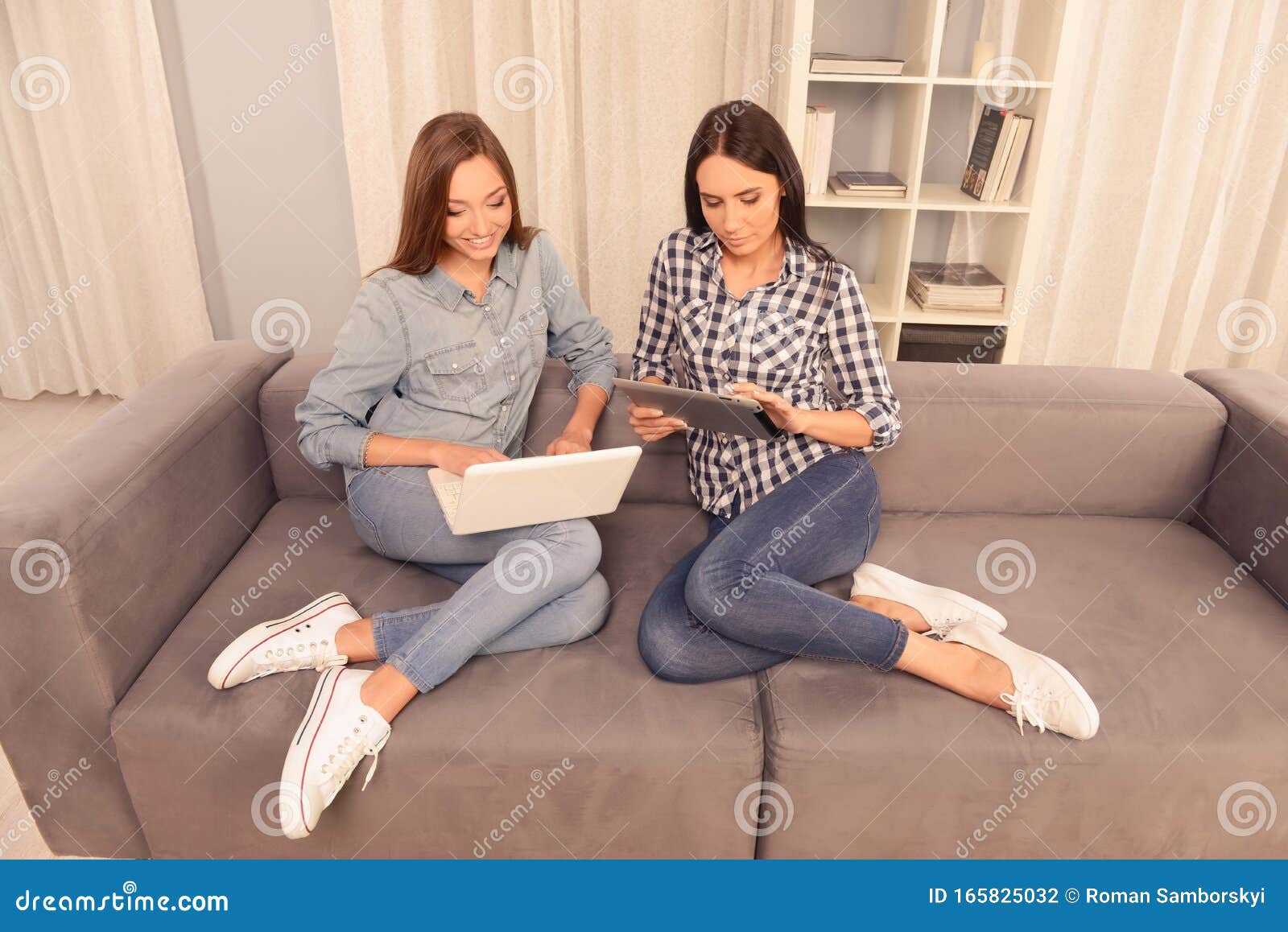 Two Pretty Girls Sitting On The Couch And Working On Laptop 库存照片 图片